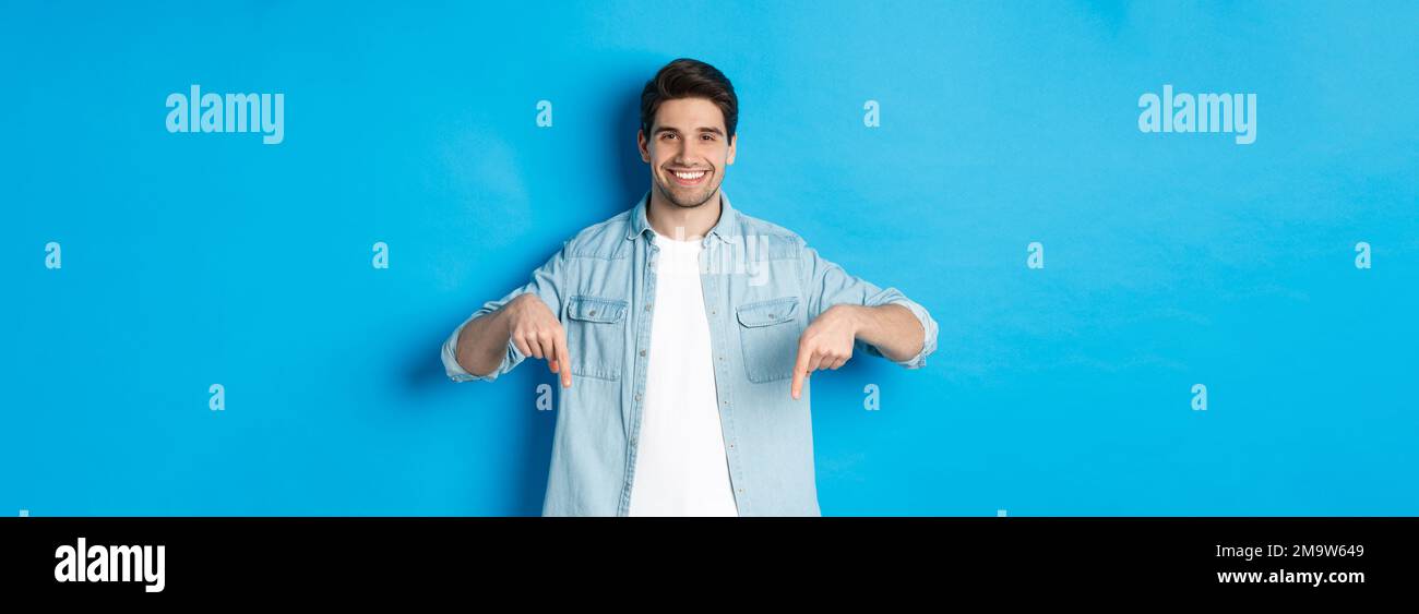 Handsome smiling adult man introduce product, pointing fingers down at ...