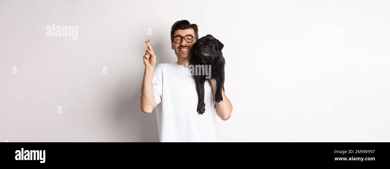Hopeful smiling dog owner making a wish, holding cute black pug on ...