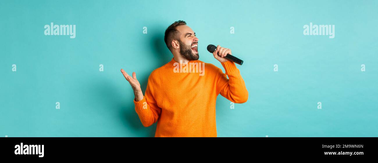 Handsome adult man perform song, singing into microphone, standing ...