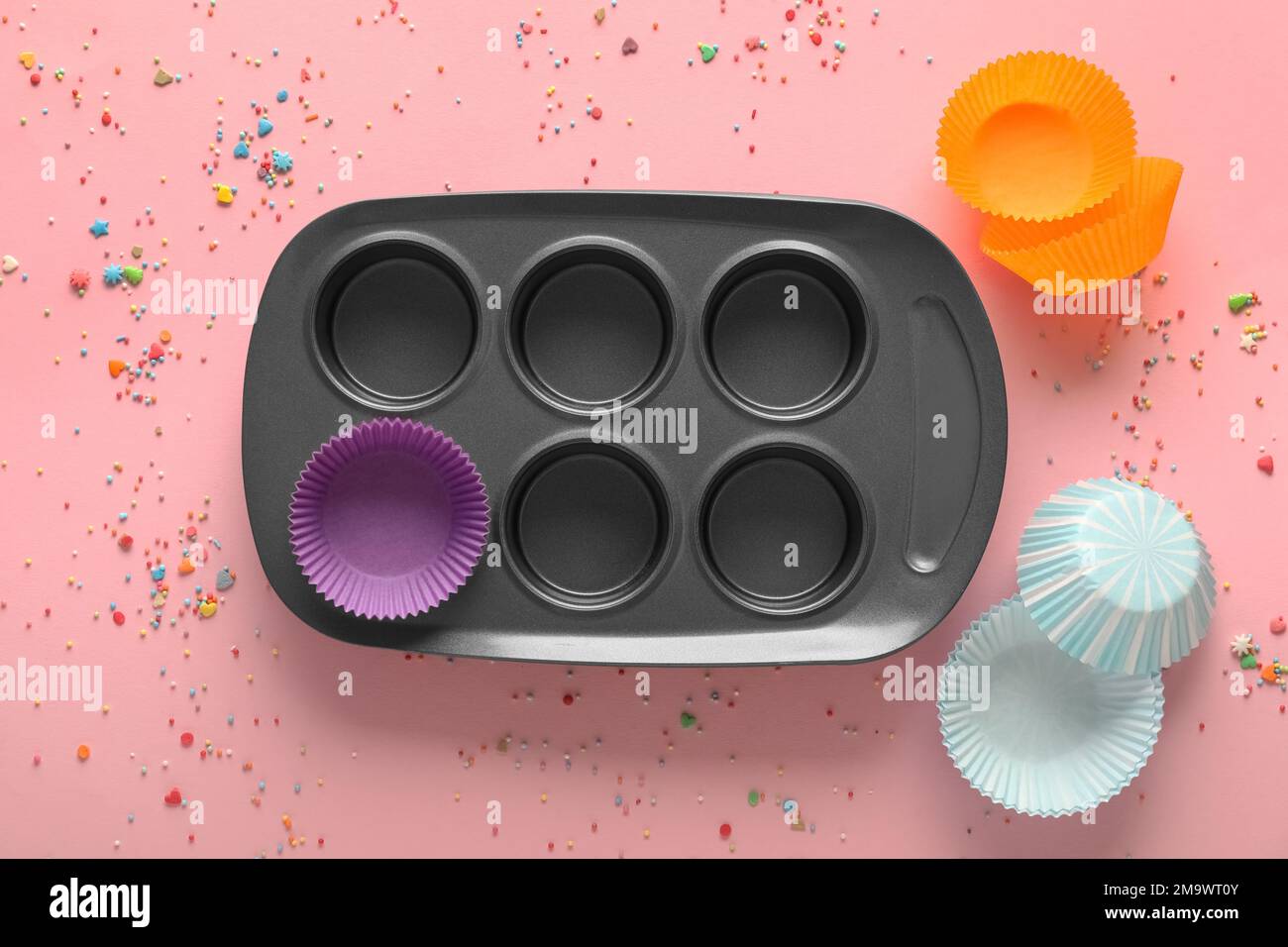 Muffin baking tray with paper forms and sprinkles on pink background ...