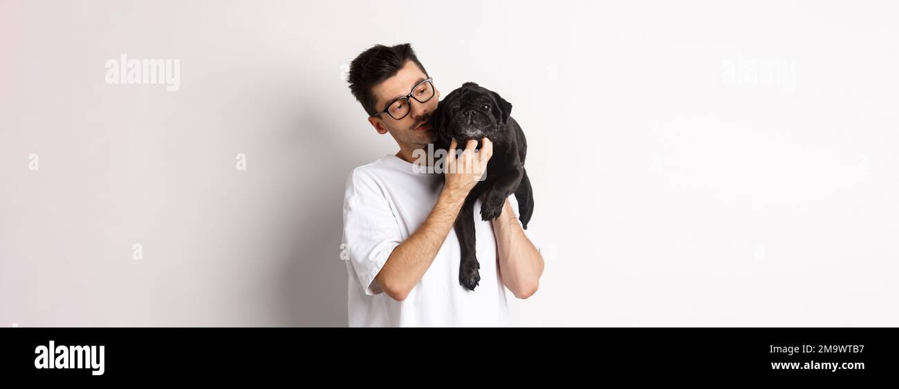 Handsome young man pet his cute black dog, scratching pug while holding ...