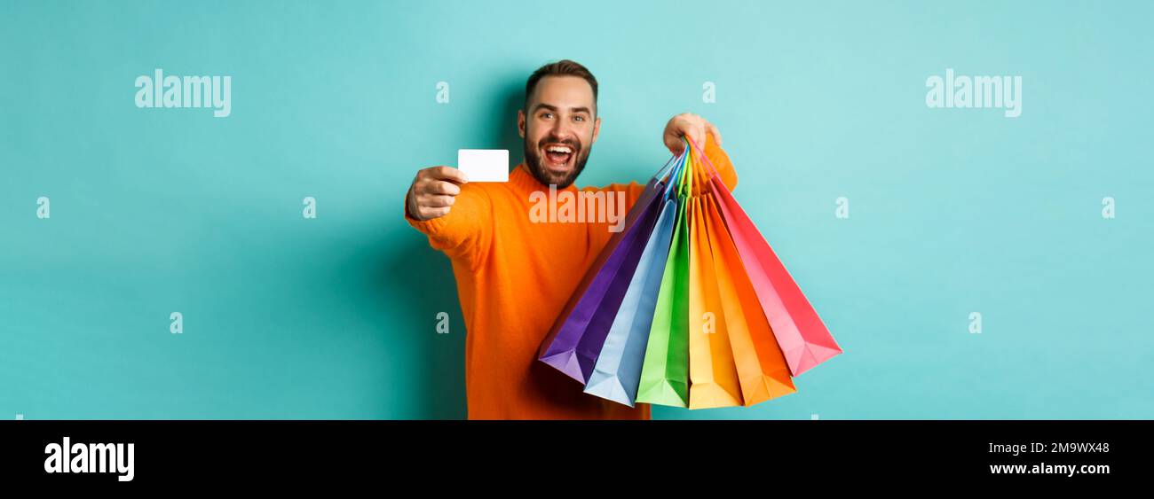 Happy aduly man showing credit card and shopping bags, standing against ...