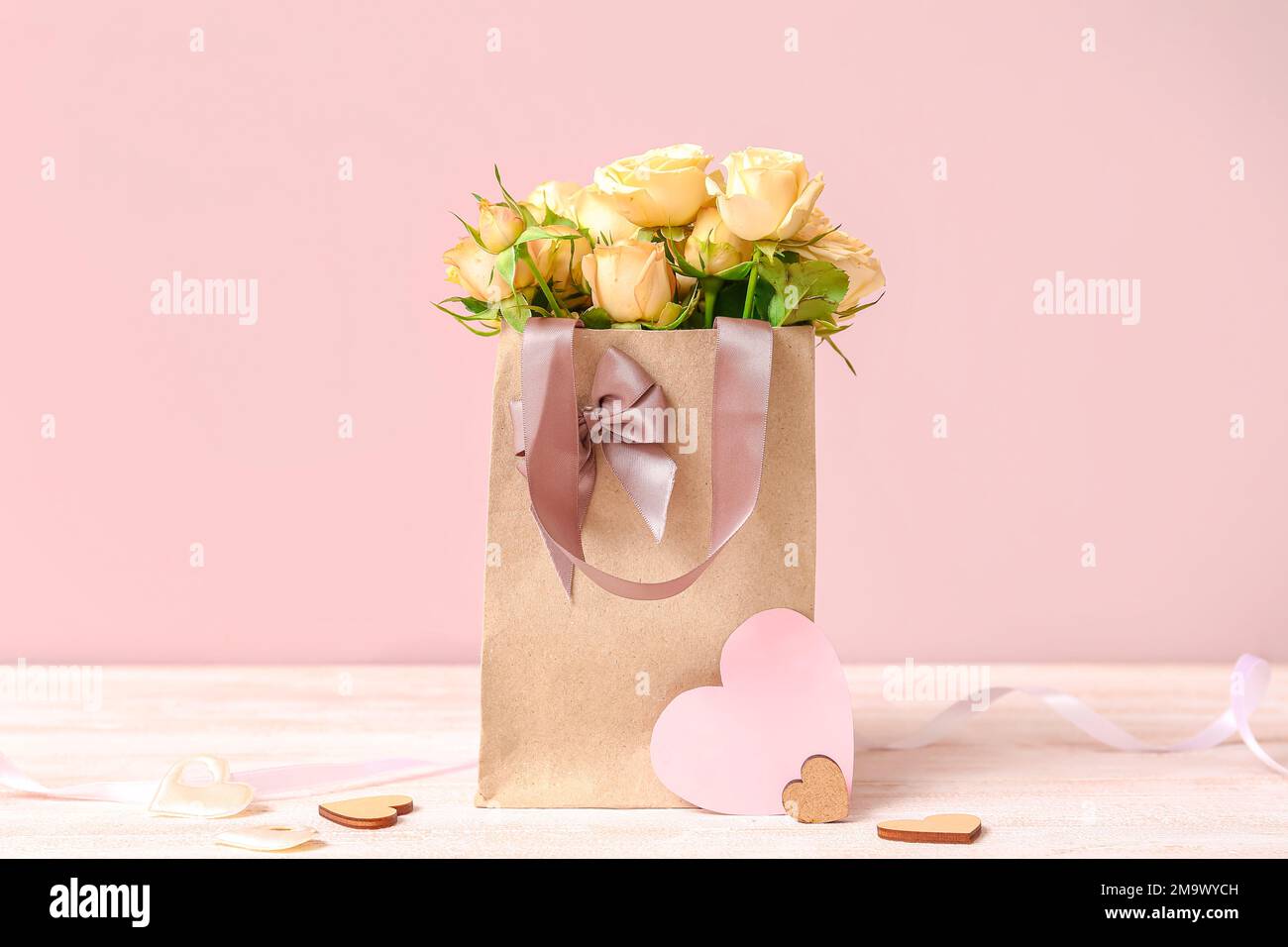 Paper bag with beautiful rose flowers on table near pink wall Stock ...