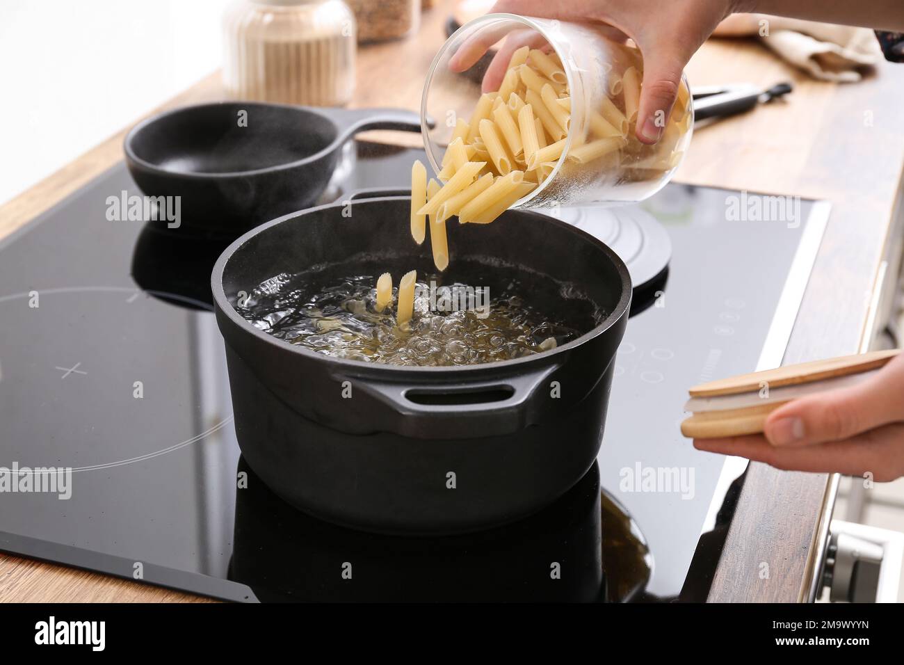 Woman pouring raw pasta into pot with boiling water on stove Stock ...