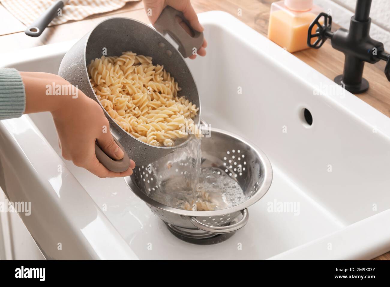 Woman pouring water from boiled pasta into colander in sink Stock Photo ...