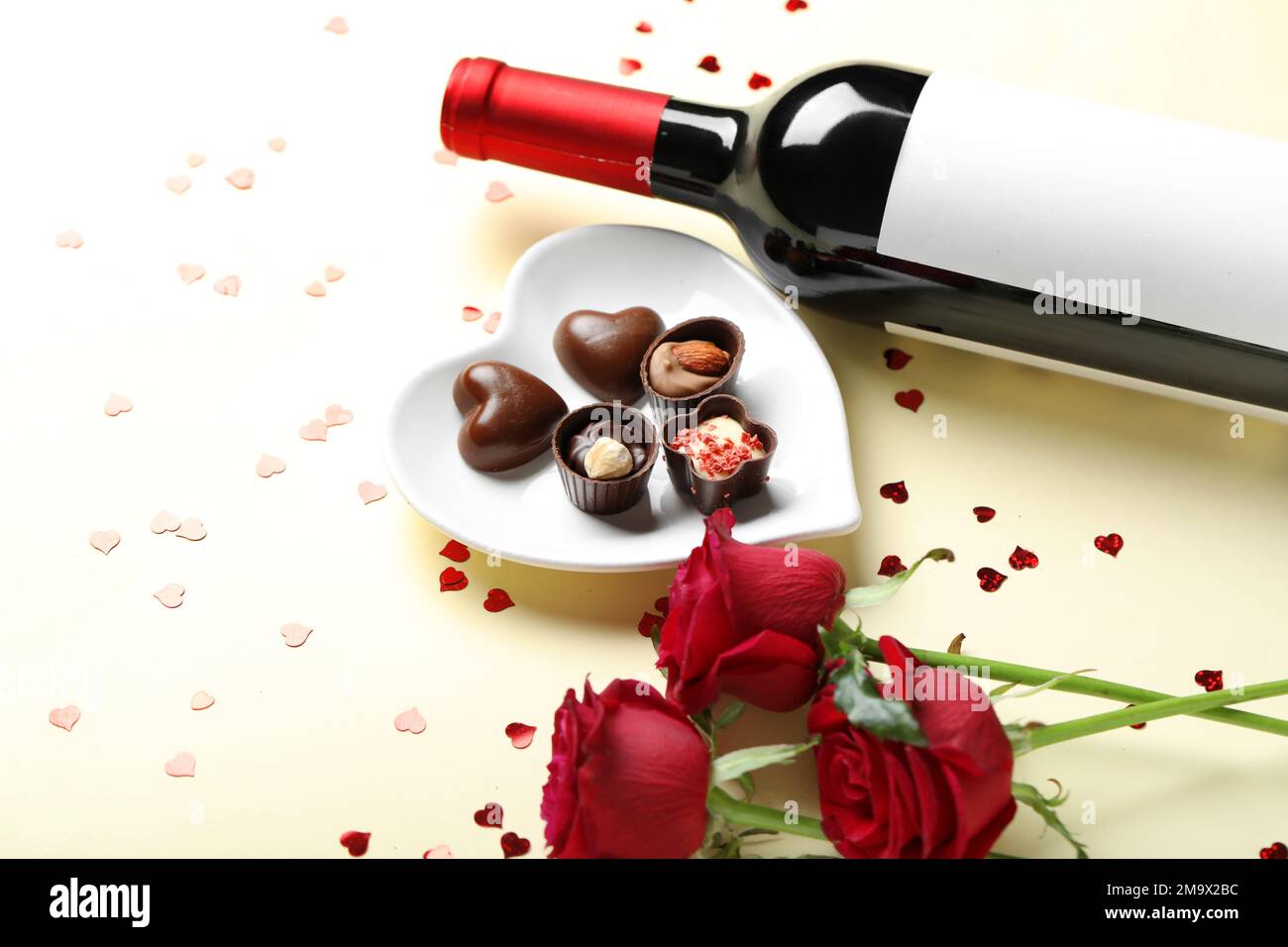 Bottle of wine, chocolate candies and rose flowers on beige background ...