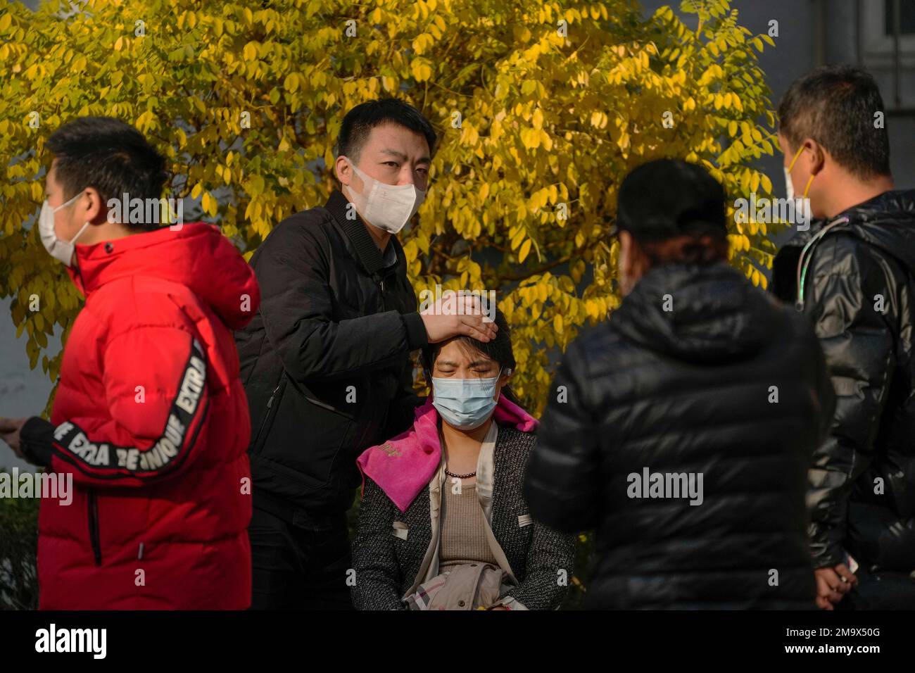 People walk by a woman wearing a face mask has her neck massage along a ...