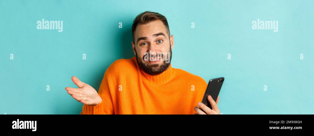 Close-up of confused man shrugging while using phone, standing ...
