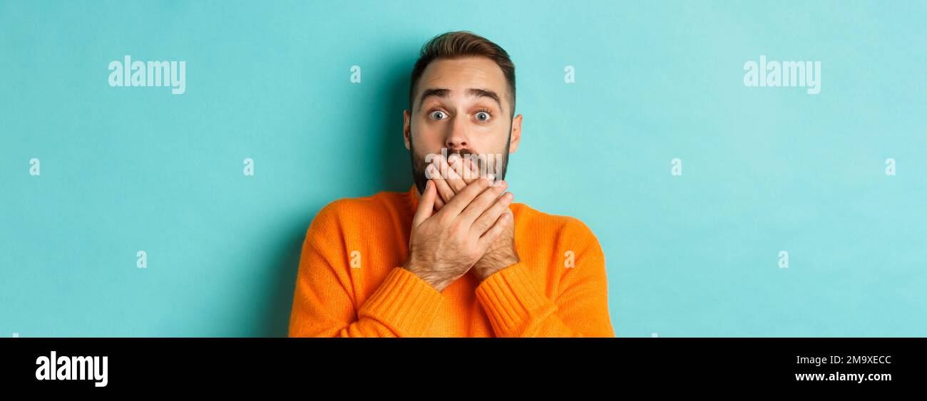 Close-up of shocked caucasian man covering his lips and mouth, staring ...
