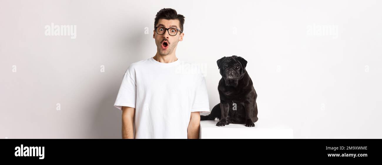 Image of dog owner and cute black pug looking at camera surprised and ...