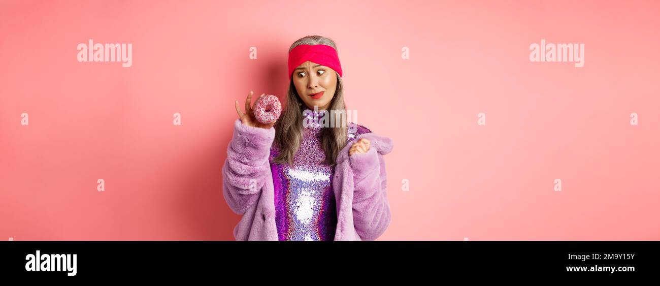 Funny asian senior woman in glittering disco dress and faux fur coat ...