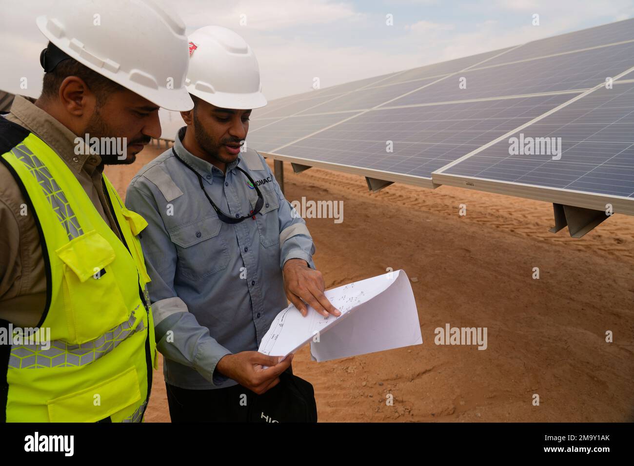Engineers talk next to photovoltaic solar panels at Benban Solar Park ...