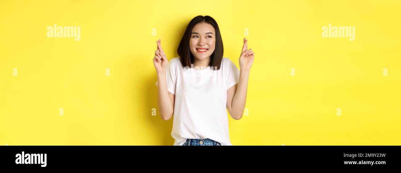 Hopeful asian girl smiling optimistic, feeling lucky, cross fingers and ...