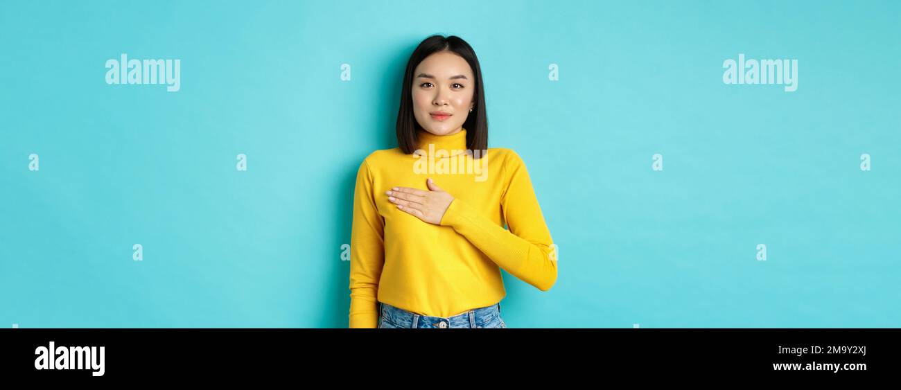 Image of proud smiling asian woman holding hand on heart, showing ...