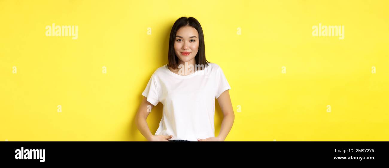 Confident and stylish asian woman holding hands on jeans and smiling ...