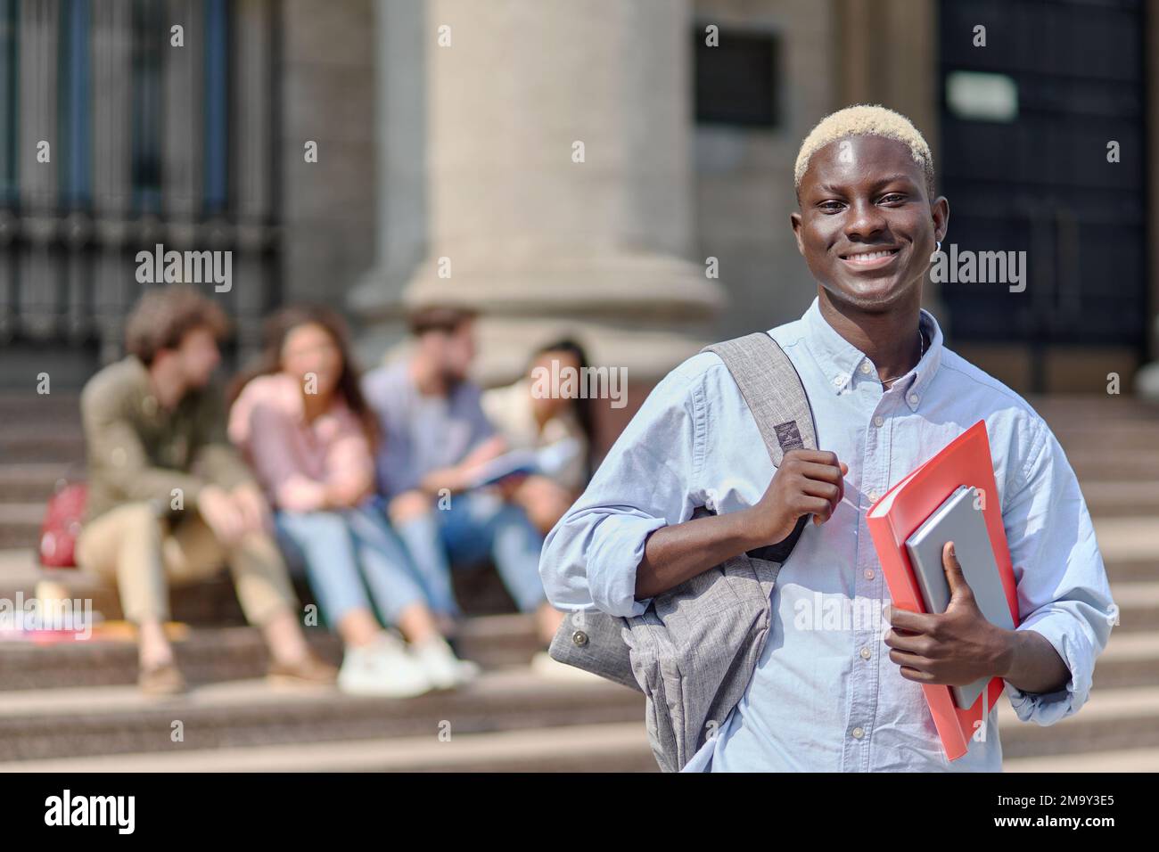 proud student with a textbook standing in front of the university ...