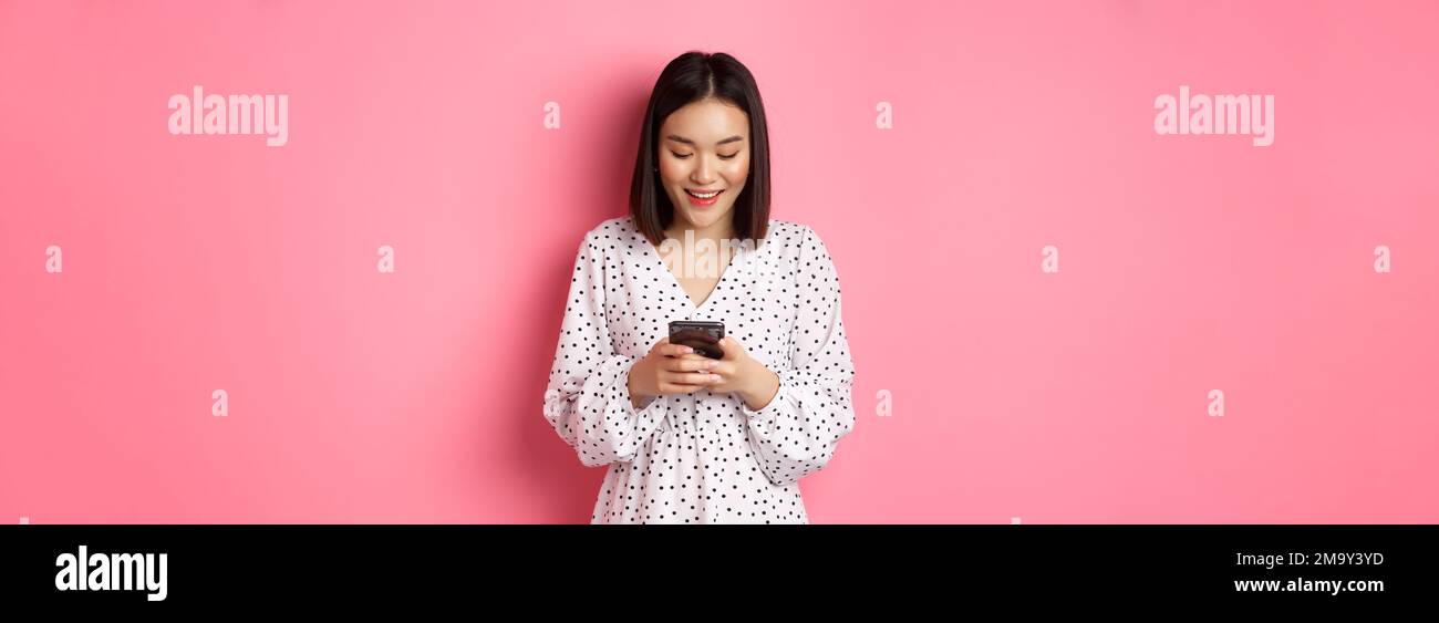 Beautiful asian lady reading message and smiling, using mobile phone ...