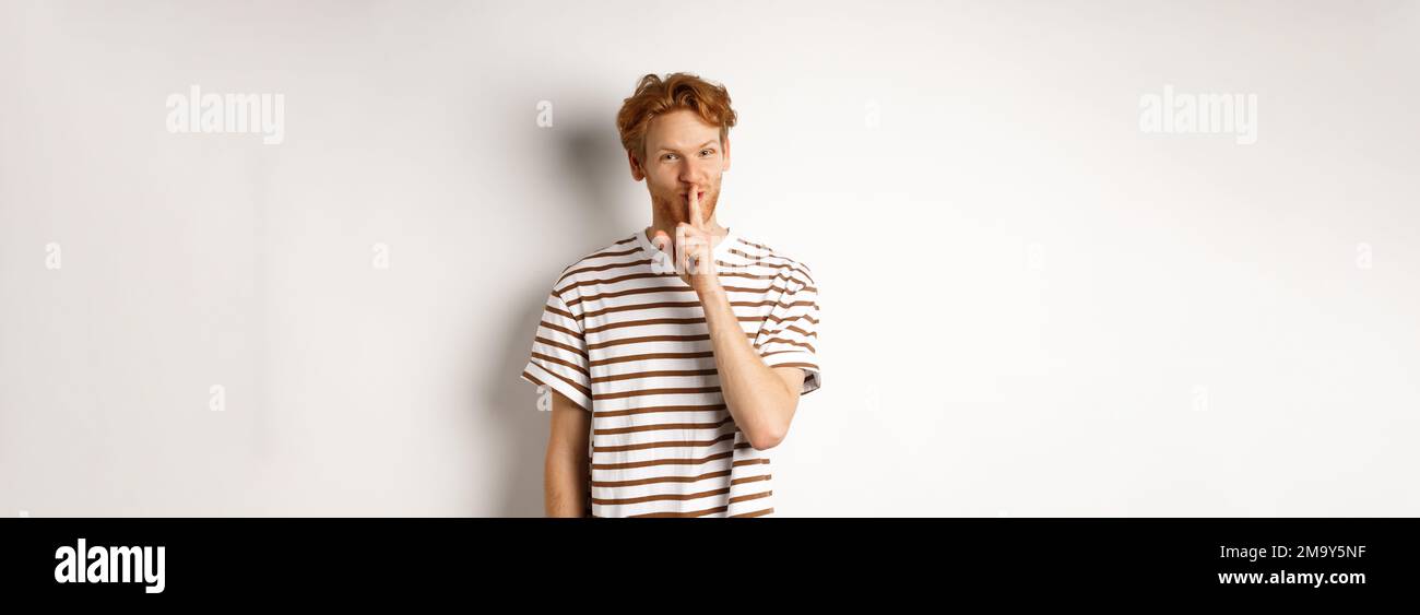 Young man student with red hair shushing, telling a secret and smiling ...