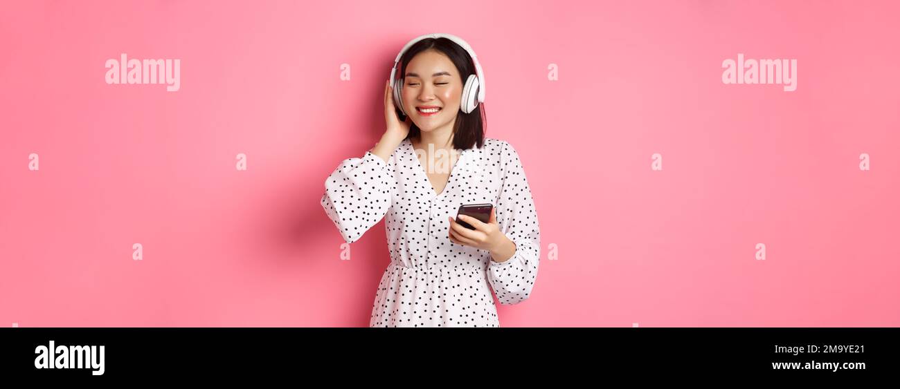 Romantic asian girl listening music in headphones, smiling with closed ...