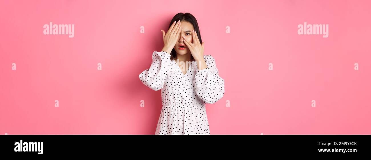 Disappointed asian woman peeking through fingers, open eyes and ...