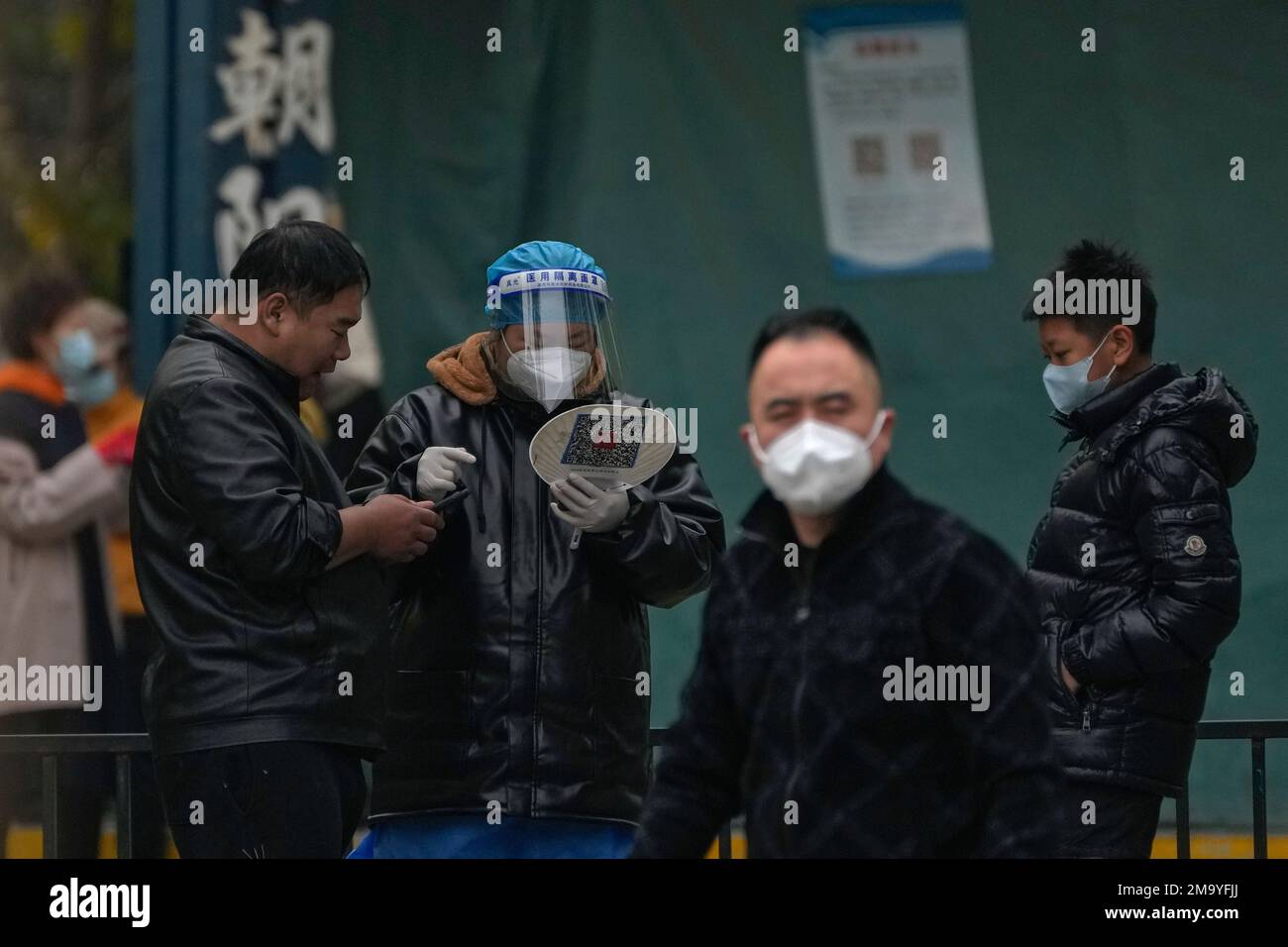 A worker in protective clothing helps a man on his health check QR ...