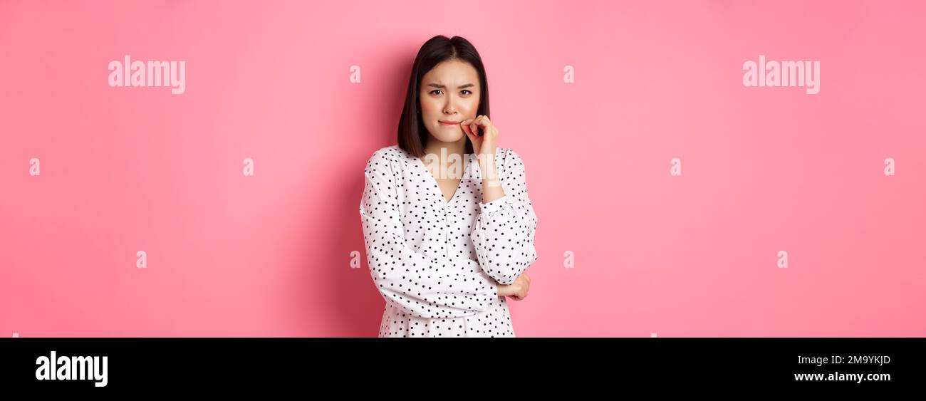 Brunette asian woman in dress looking displeased, frowning and zipping ...