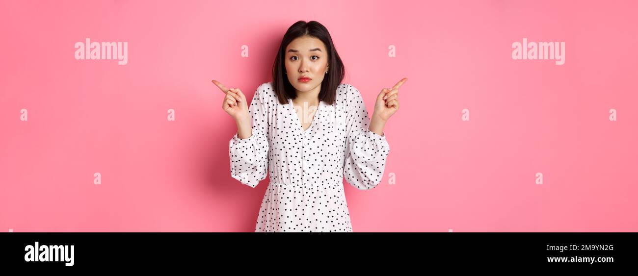 Confused asian woman hesitating, shrugging and pointing hands two sides ...
