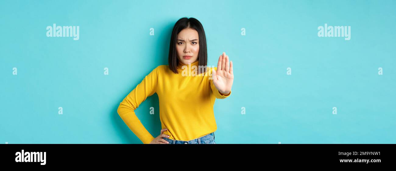 Confident and serious asian woman tell no, showing stop gesture to ...