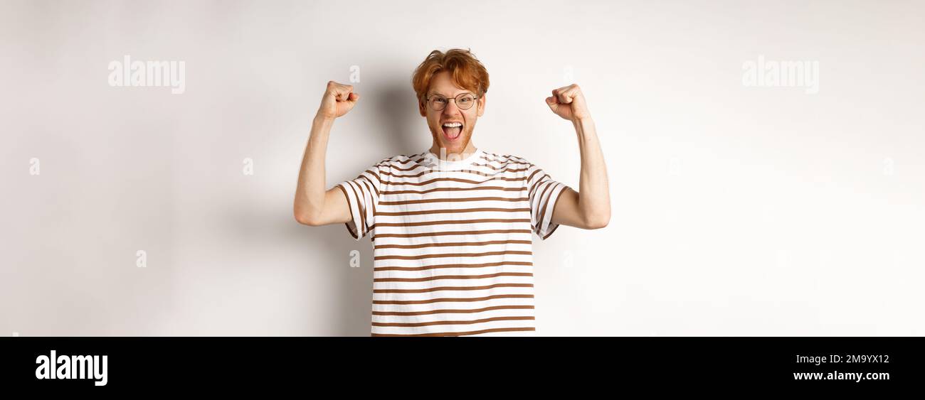 Joyful redhead guy raising hands up like winner, winning prize and ...
