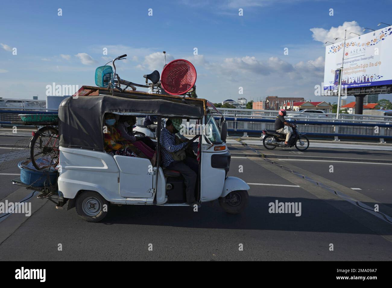 A motorized rickshaw drives past a billboard advertising the upcoming ...