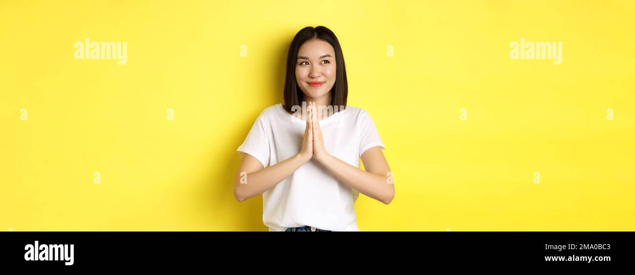Pretty asian woman holding hands in namaste, pray gesture, looking left ...