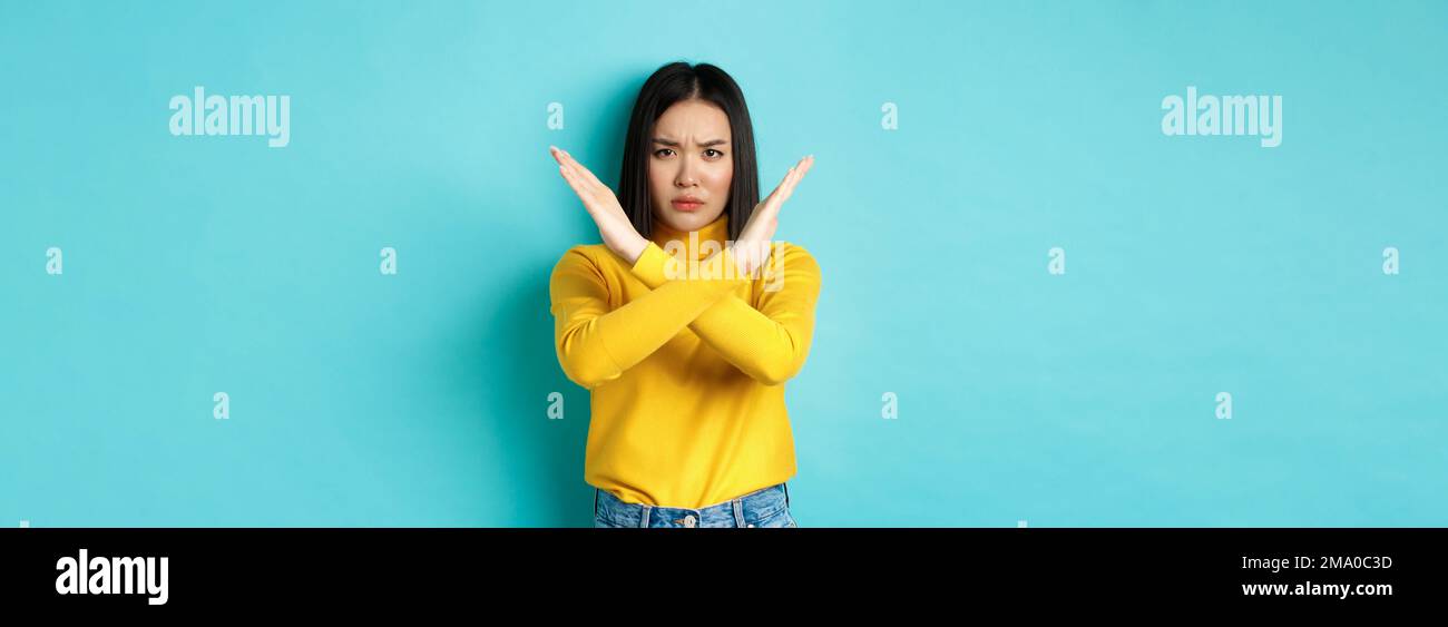 Serious and assertive korean woman showing cross stop gesture, frowning ...