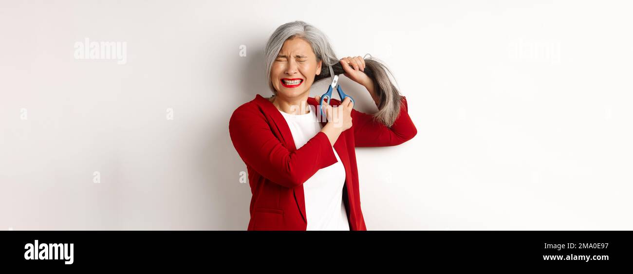 Scared asian woman cutting hair with scissors and feeling anxious ...