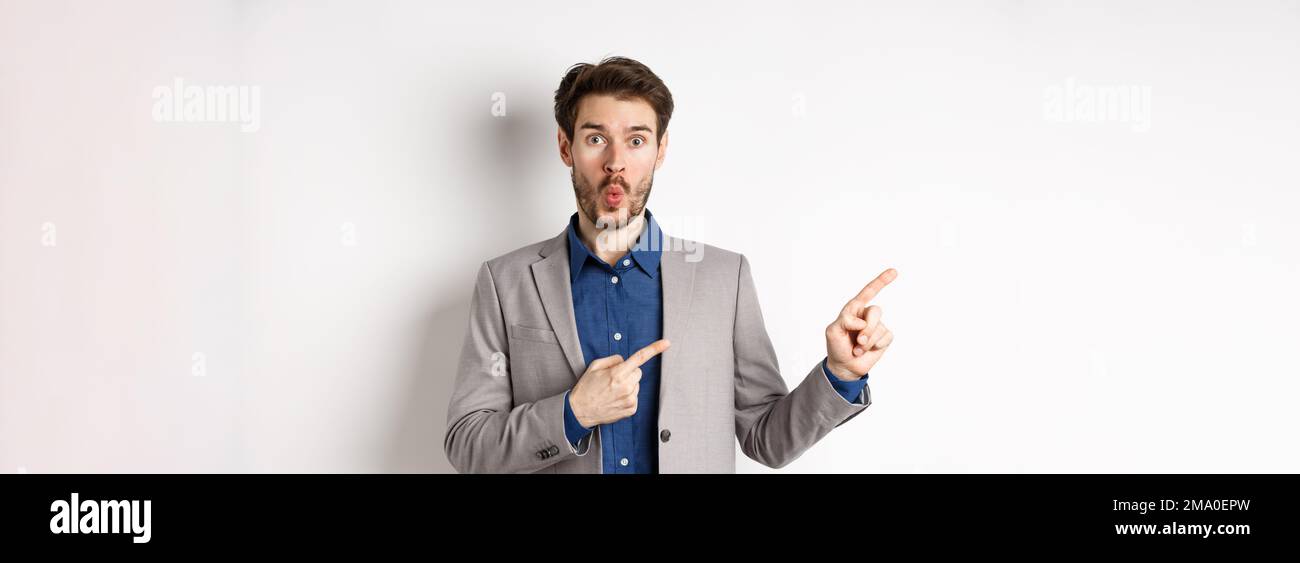 Excited handsome man in suit pointing fingers left at banner and saying ...