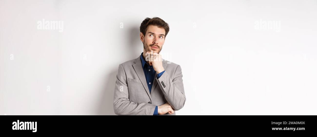 Pensive handsome man in suit looking up and thinking, making choice ...