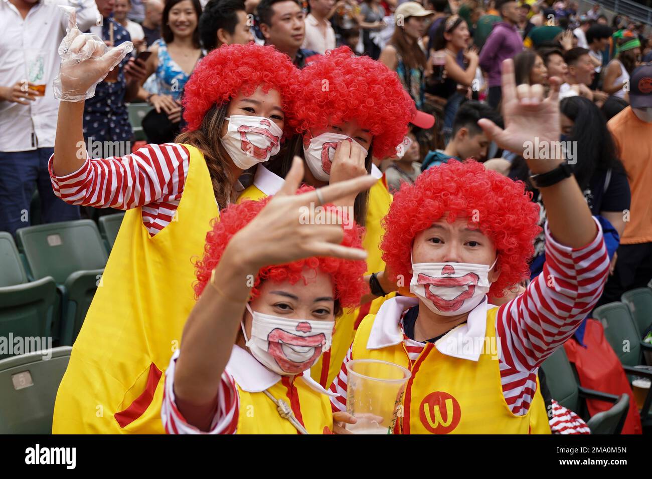 Spectators dressed in Ronald McDonald costumes gesture as they watch ...