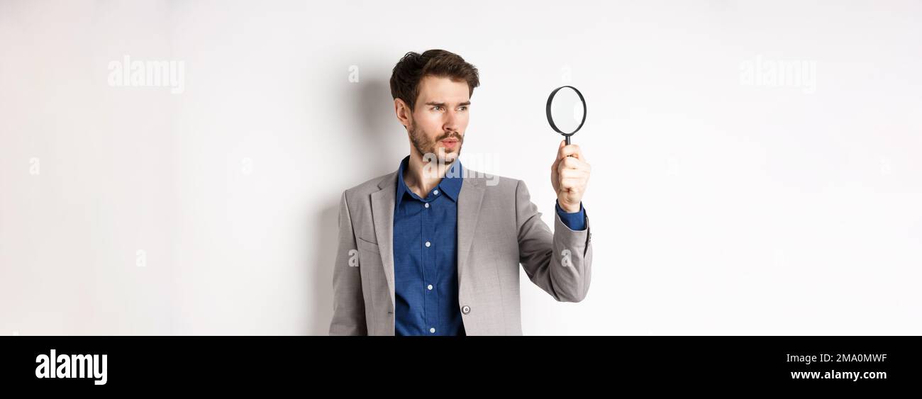 Serious man in suit searching for clues through magnifying glass ...
