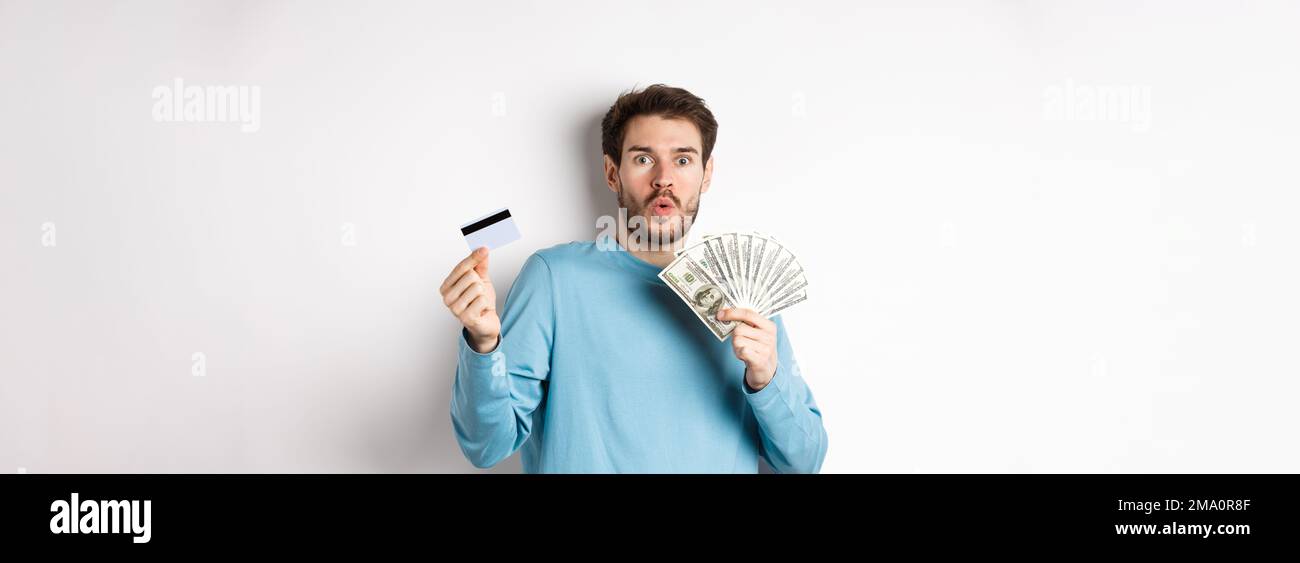 Surprised young man showing money in dollars and plastic credit card ...