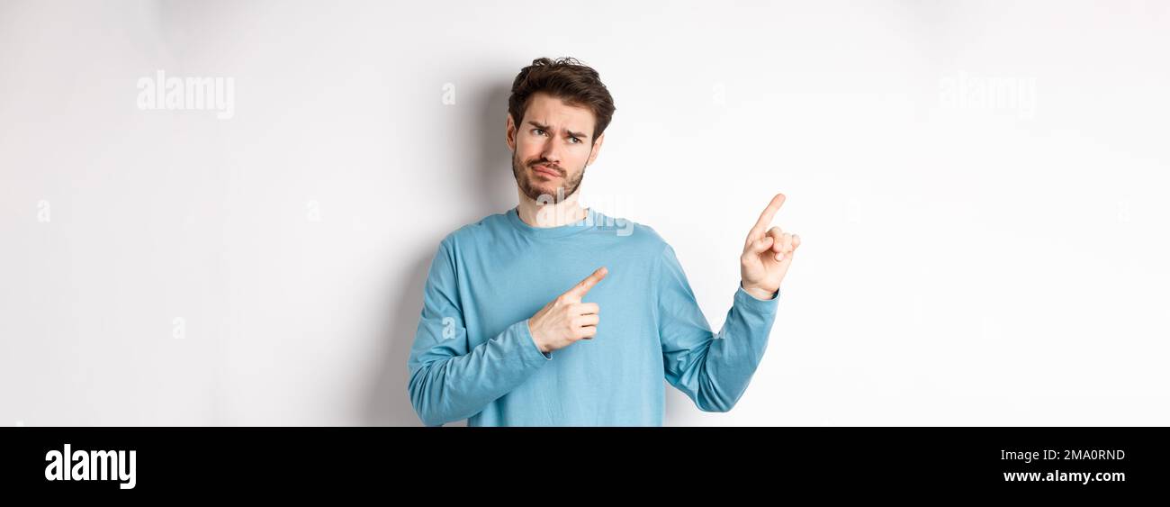 Skeptical and unimpressed young man grimacing, pointing fingers and ...