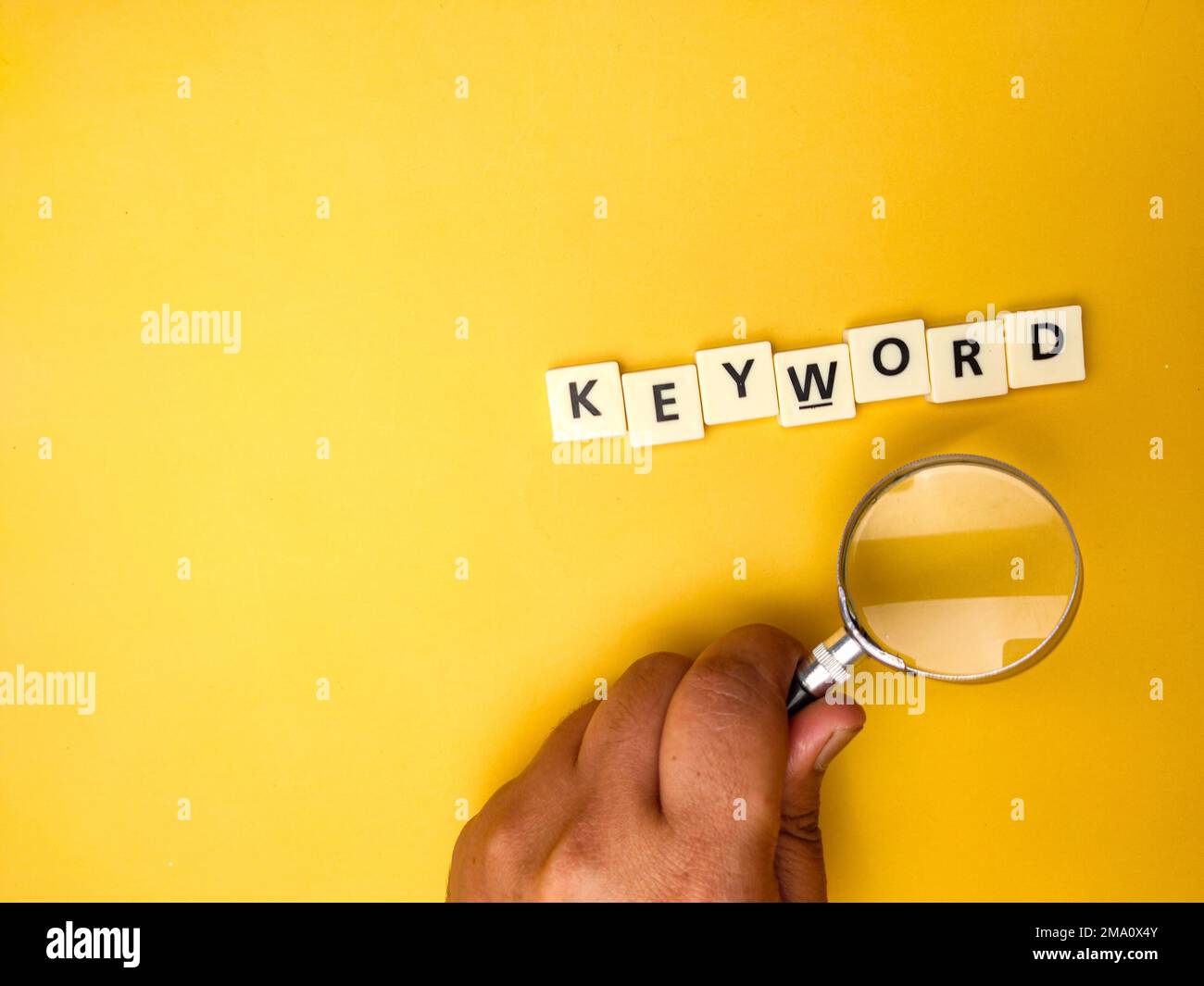 Hand holding magnifying glass with the word KEYWORD on yellow ...