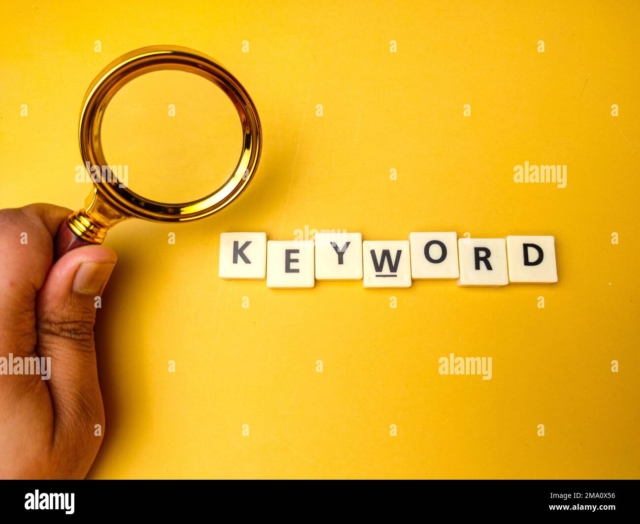 Hand holding magnifying glass with the word KEYWORD on yellow ...