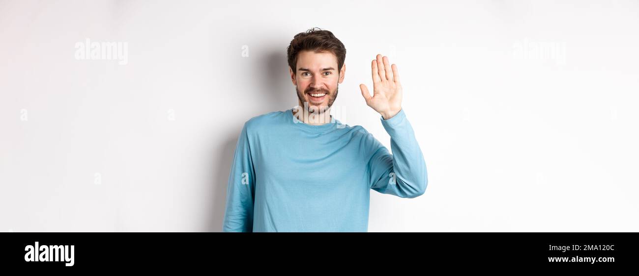 Cheerful young man with beard saying hello, looking friendly and waving ...