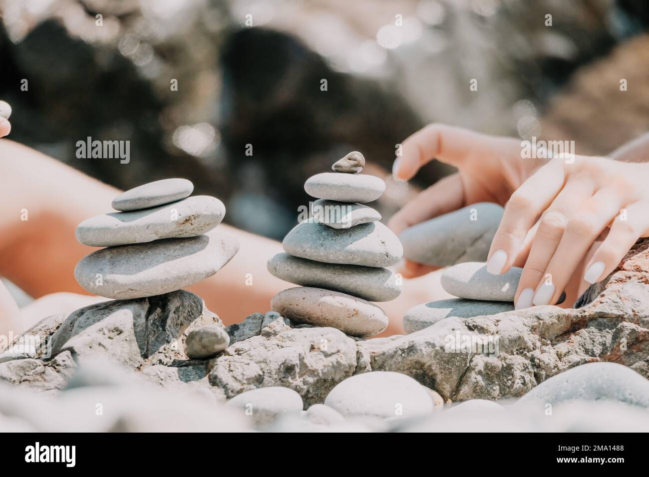 Woman with daughter bilds stones pyramid on seashore on a sunny day on ...