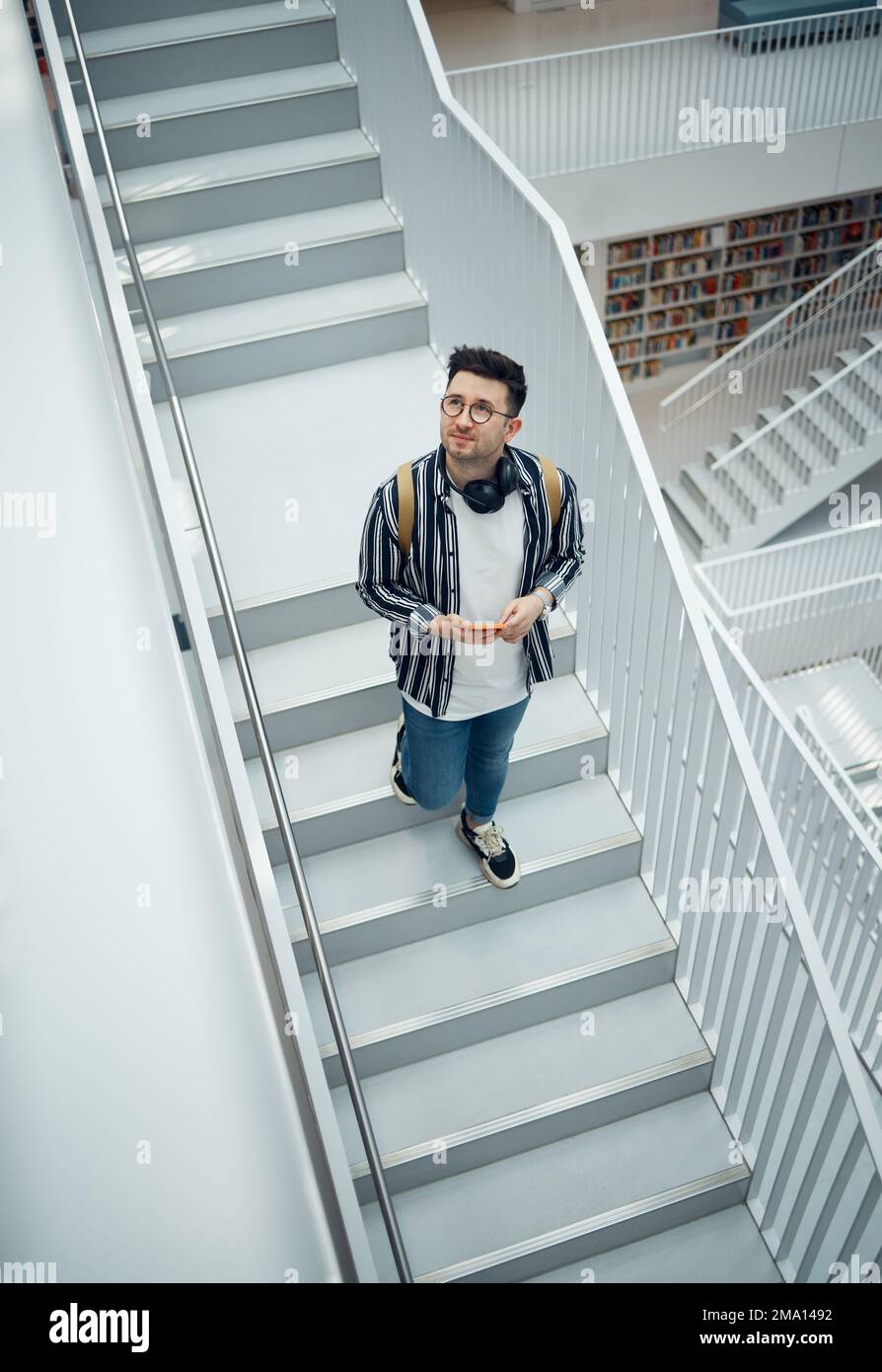 Library, staircase and student man walking in a education, learning and ...