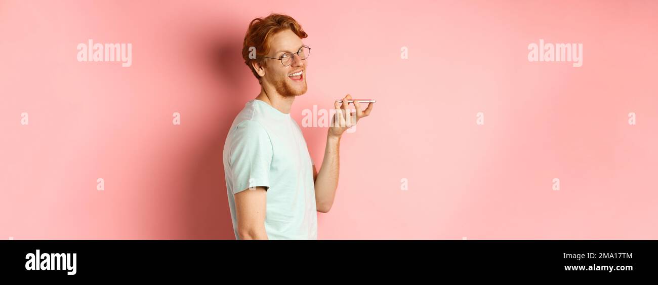 Handsome young man standing in profile and talking on speakerpone ...