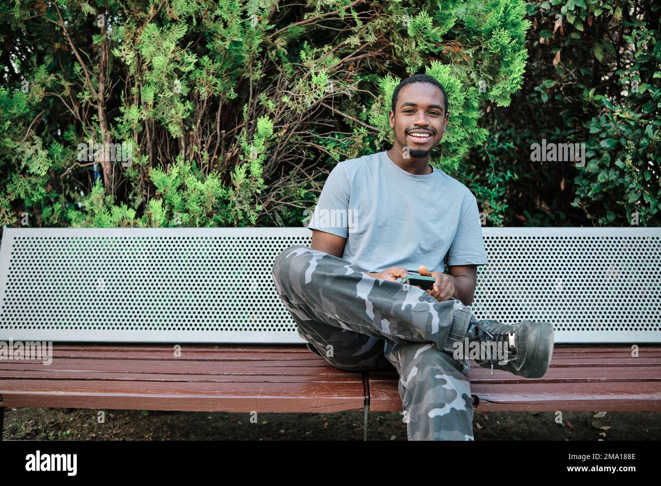 Man looking at camera and smiling while using mobile phone sitting on a ...