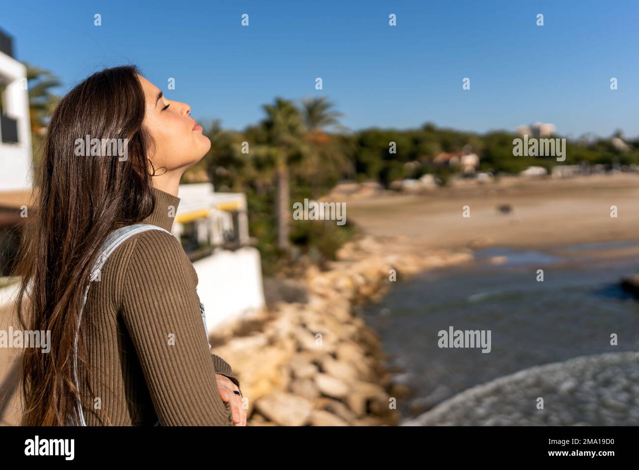 Side view of serene Hispanic lady standing on seacoast and closing eyes ...