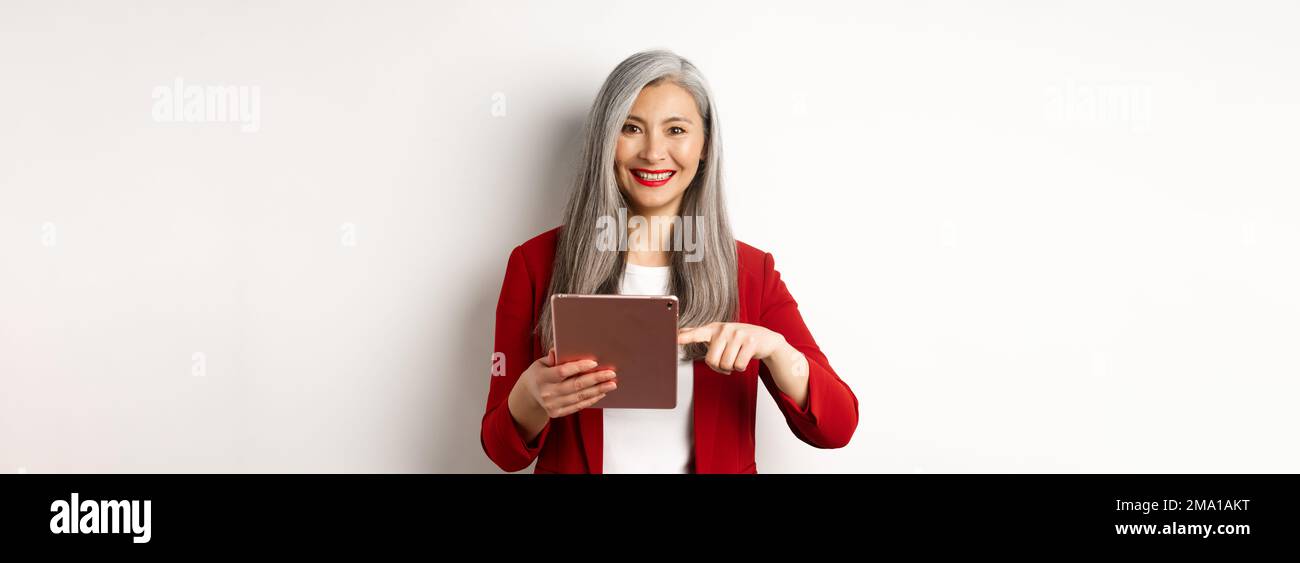 Business. Smiling senior businesswoman using digital tablet, pointing ...