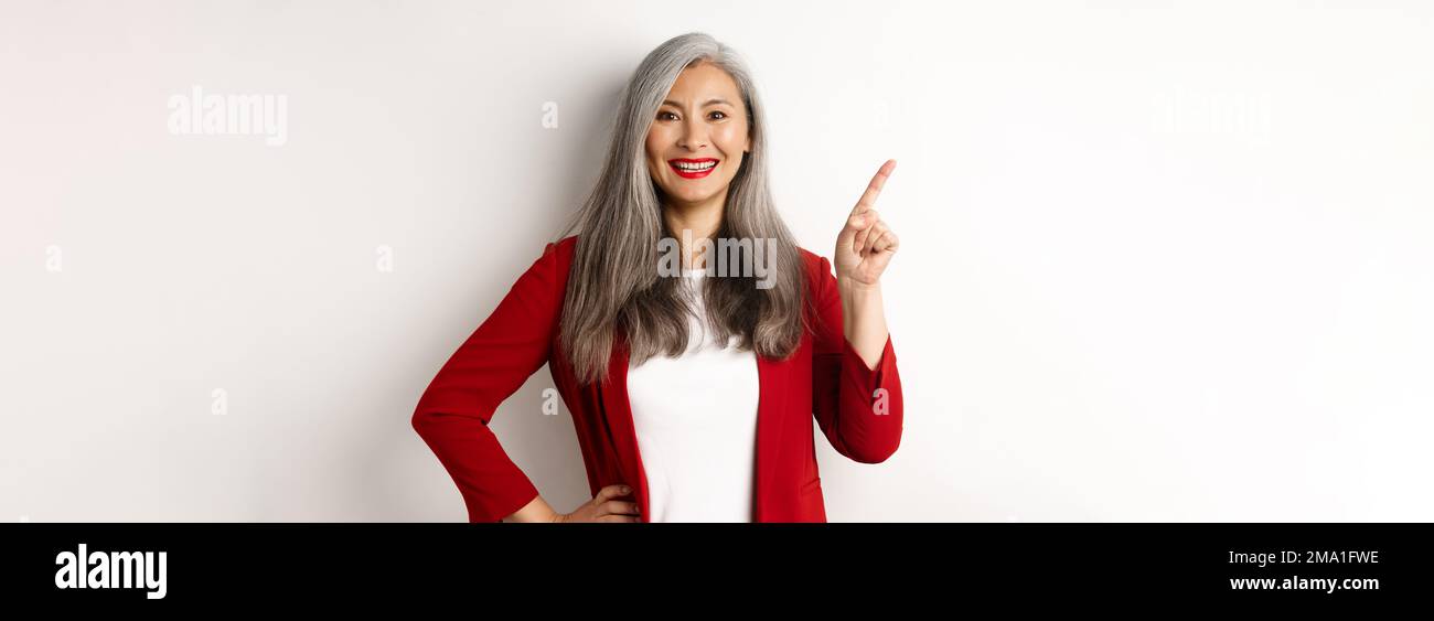 Happy senior office lady pointing finger at upper left corner, showing ...