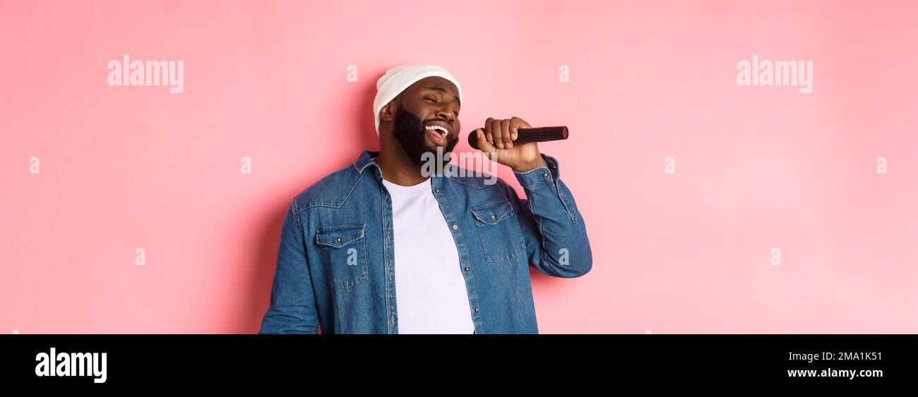 Handsome Black man in beanie and denim shirt singing karaoke, holding ...